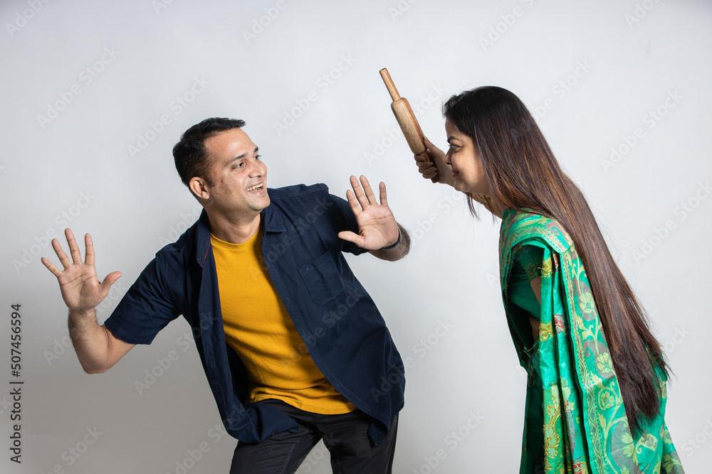 Angry young indian woman holding rolling pin hitting her husband ...