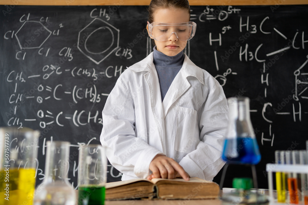 little scientist girl with glasses in lab coat mixing chemical liquids ...