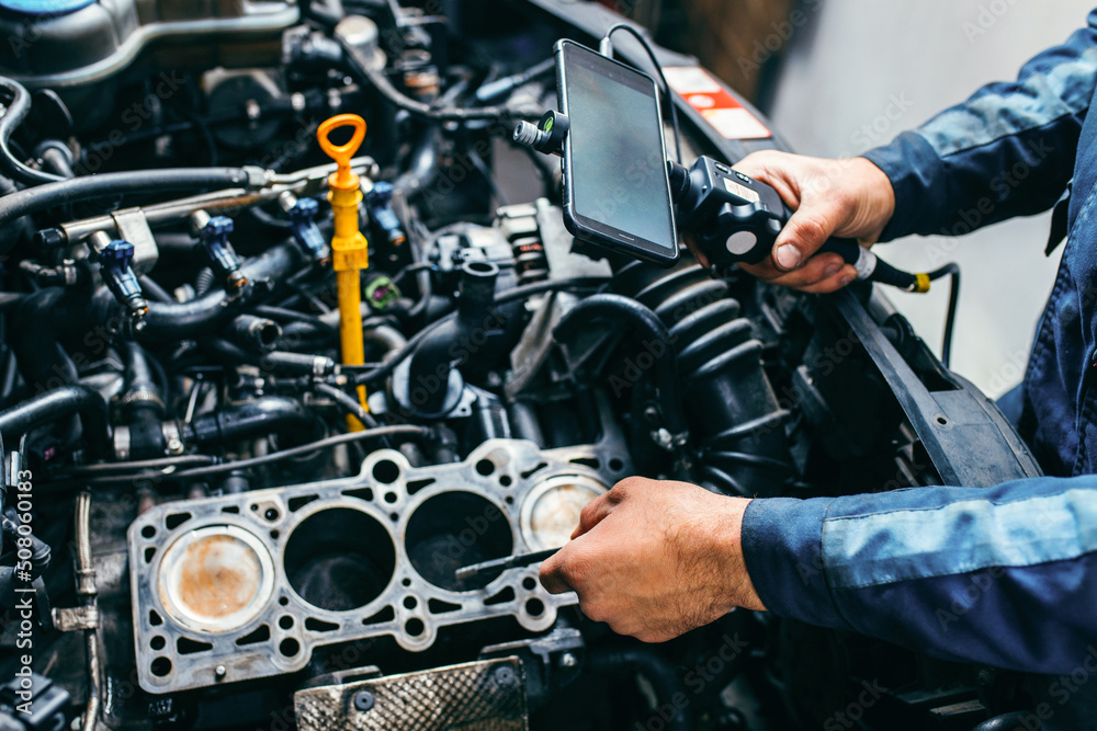 Hands of car mechanic check the vehicle engine with technical endoscope ...