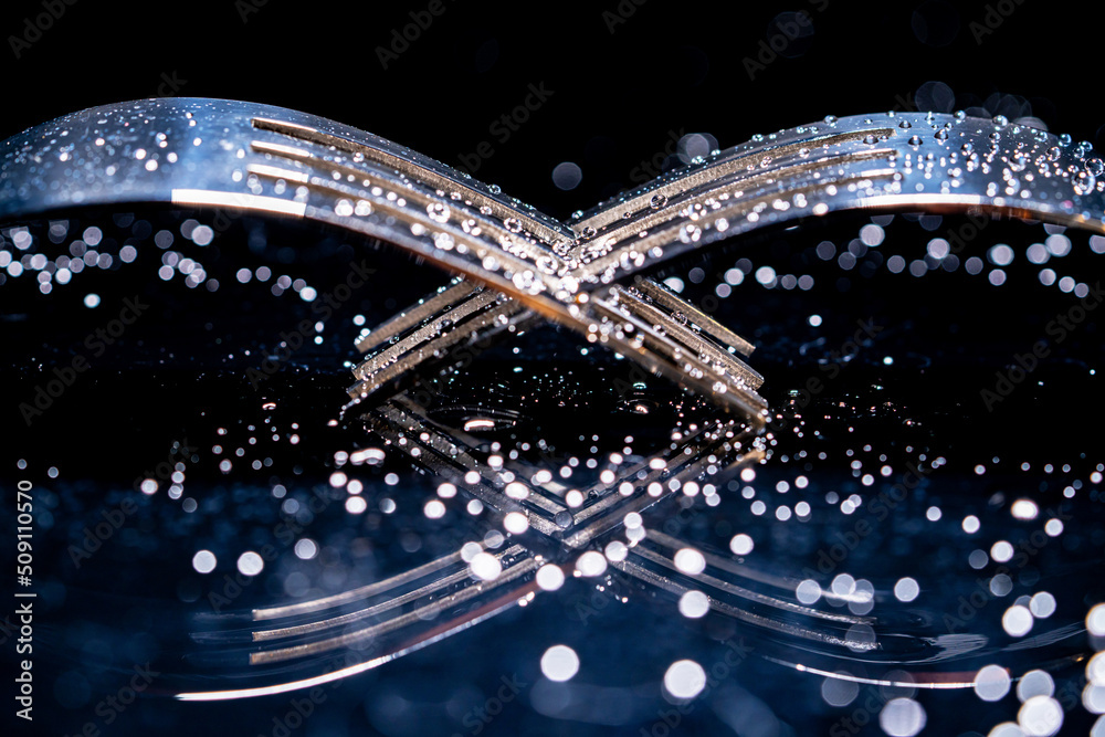 Two interlocking forks with drops of water reflecting off a glossy ...