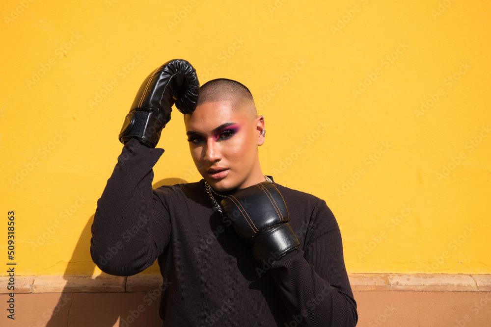 Young non-binary person wears boxing gloves on a mustard yellow ...