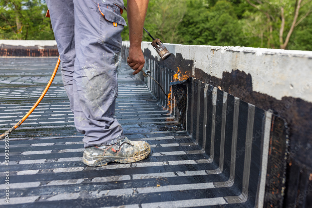 Workers placing a vapor barrier on the roof using a propane gas torch ...