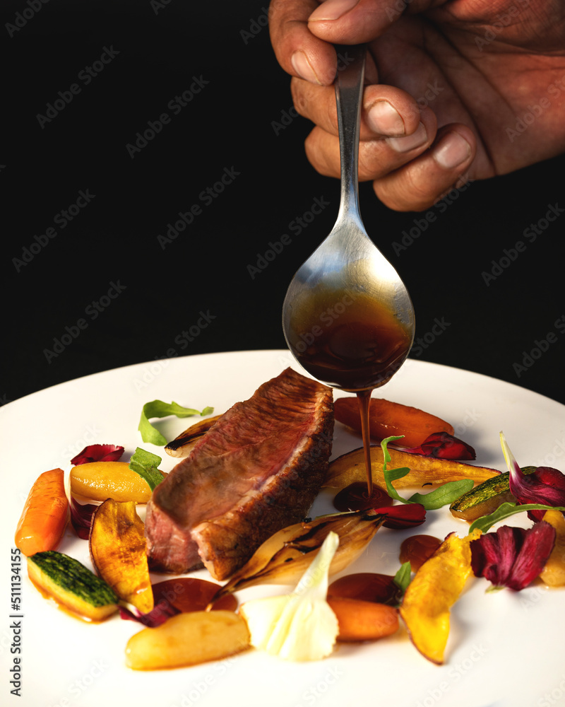 medium rare lamb meat with cooked vegetables, petals and hand pouring ...