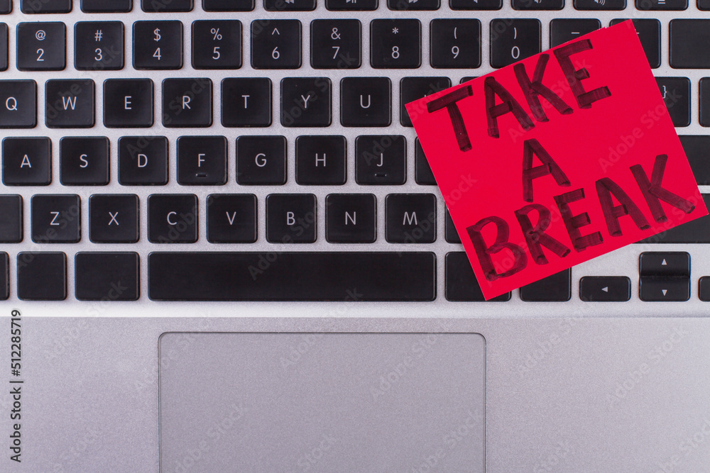 Sticker note on laptop keyboard saying take a break. Comfort work place ...