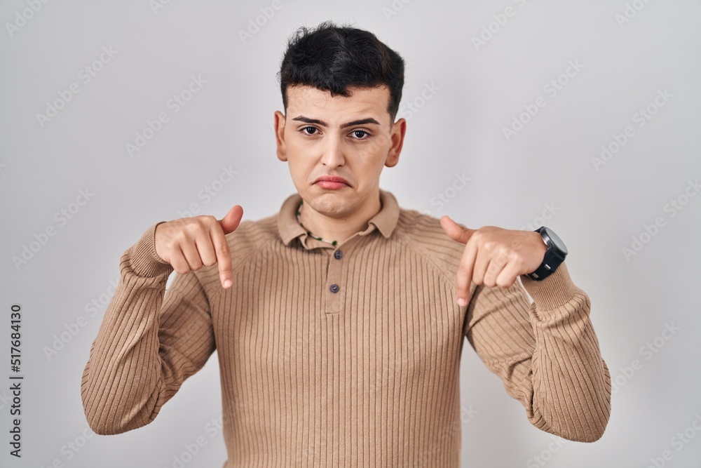 Non binary person standing over isolated background pointing down ...