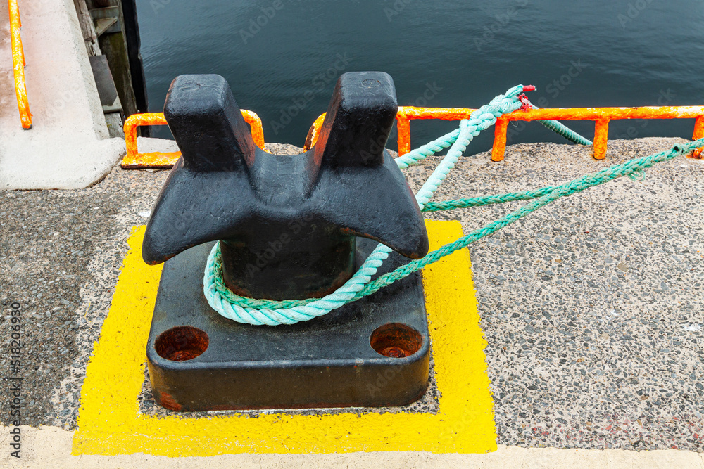 Mooring cable tied to an iron bollard on a concrete dock, boat cable ...