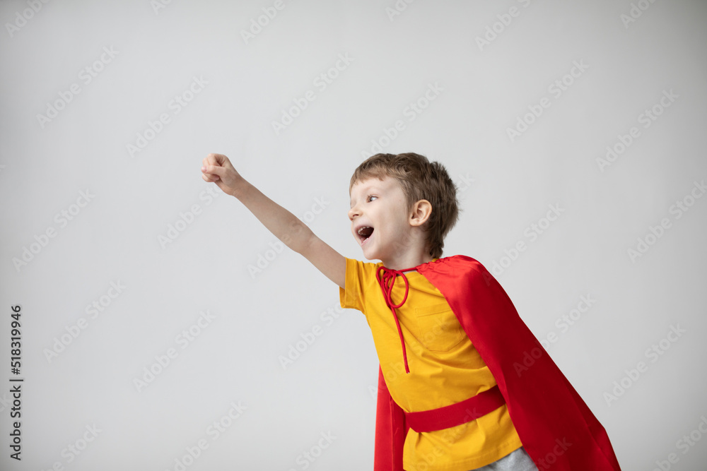 Cheerful child is playing in superhero in red cloak, holding out his ...