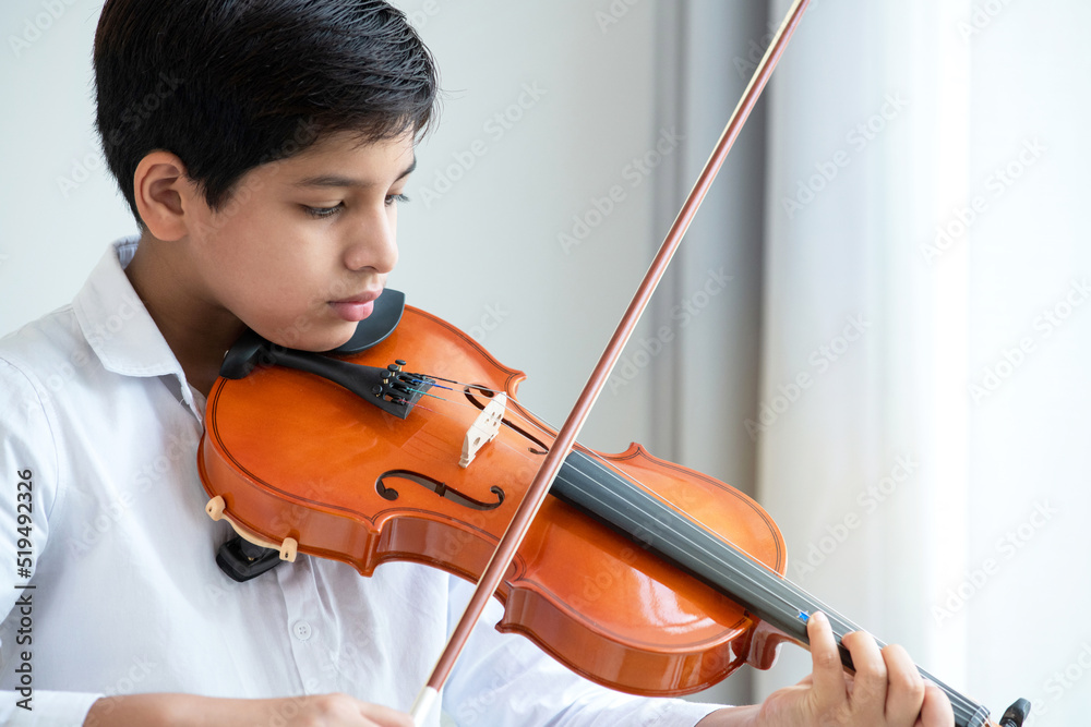 Indian boy practicing playing violin at home, holds the violin ...