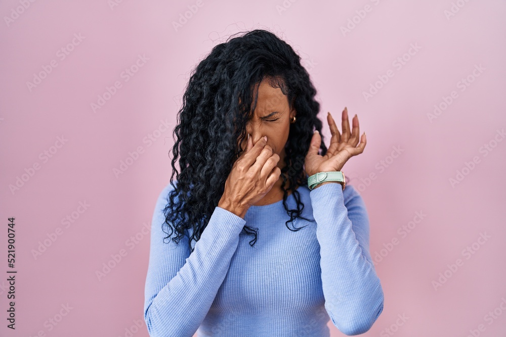 Middle age hispanic woman standing over pink background smelling ...