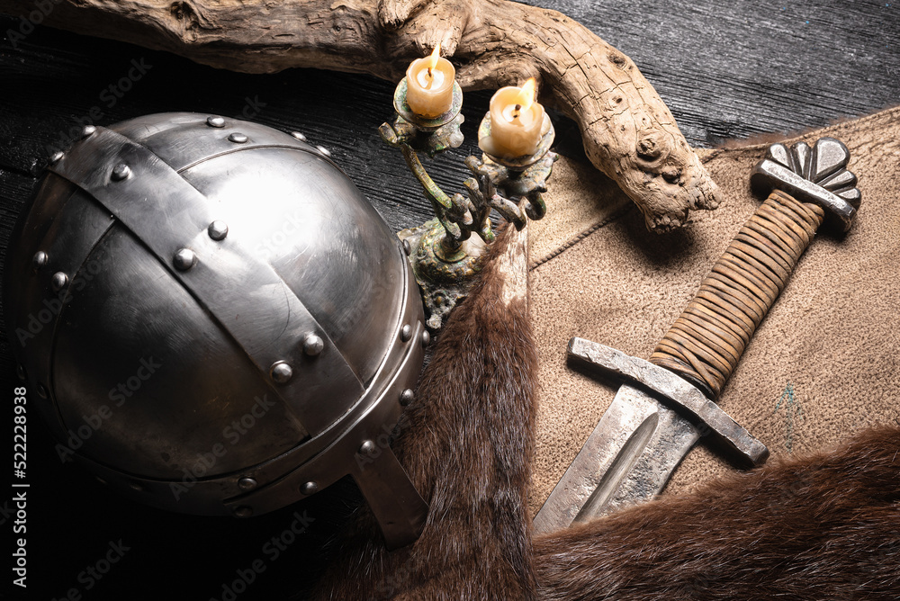 Viking sword, helmet and animal fur skin on the old wooden table close ...
