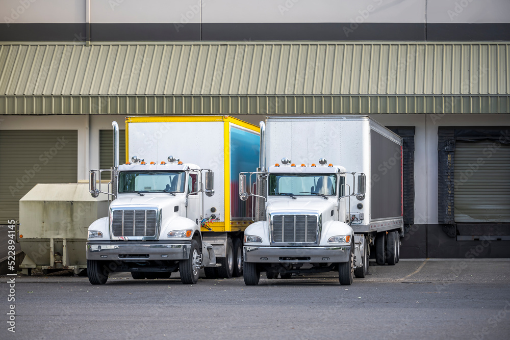 Foto Compact middle duty rigs semi trucks with box trailers standing in ...