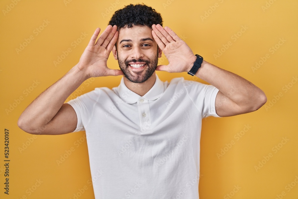 Arab man standing over yellow background smiling cheerful playing peek ...