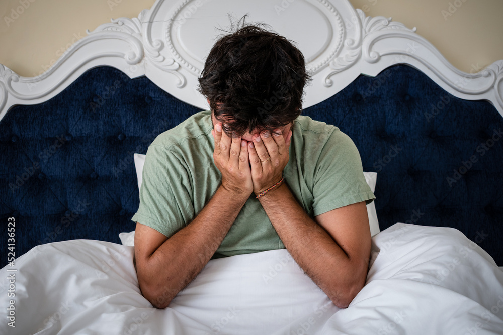 Hombre levantandose de la cama con depresión y malestar, cubriendose la ...