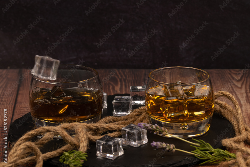 two liqueur glasses of whisky, rum, añejo, ice falling in glass tumbler ...