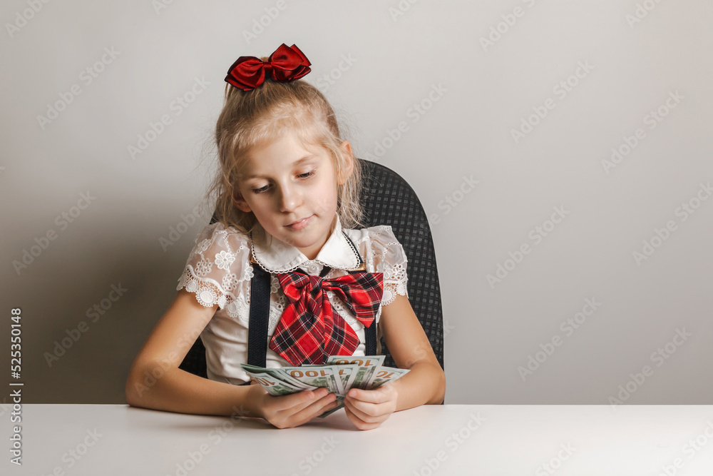 Little girl in school uniform holds a fan of hundred dollar bills ...