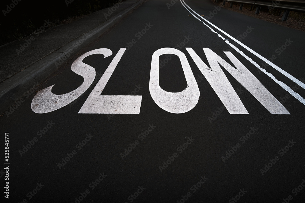 SLOW road sign painted on bitumen asphalt road in white paint ...