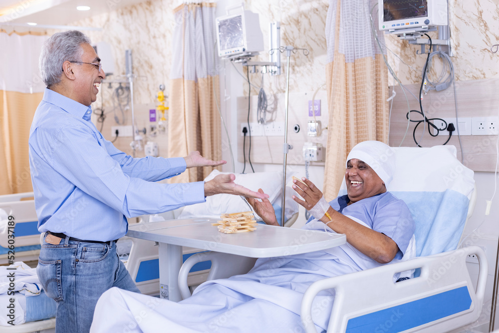 Senior patient playing wooden blocks with his friend lying on bed at ...