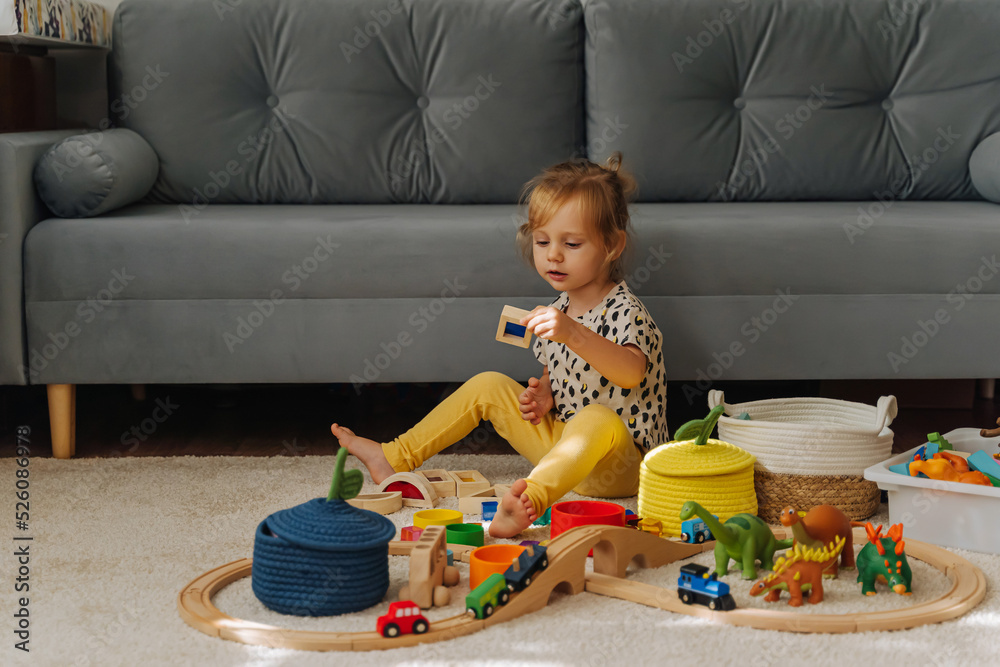 Kid girl builds a toy town and wooden railway. A little girl sitting on ...