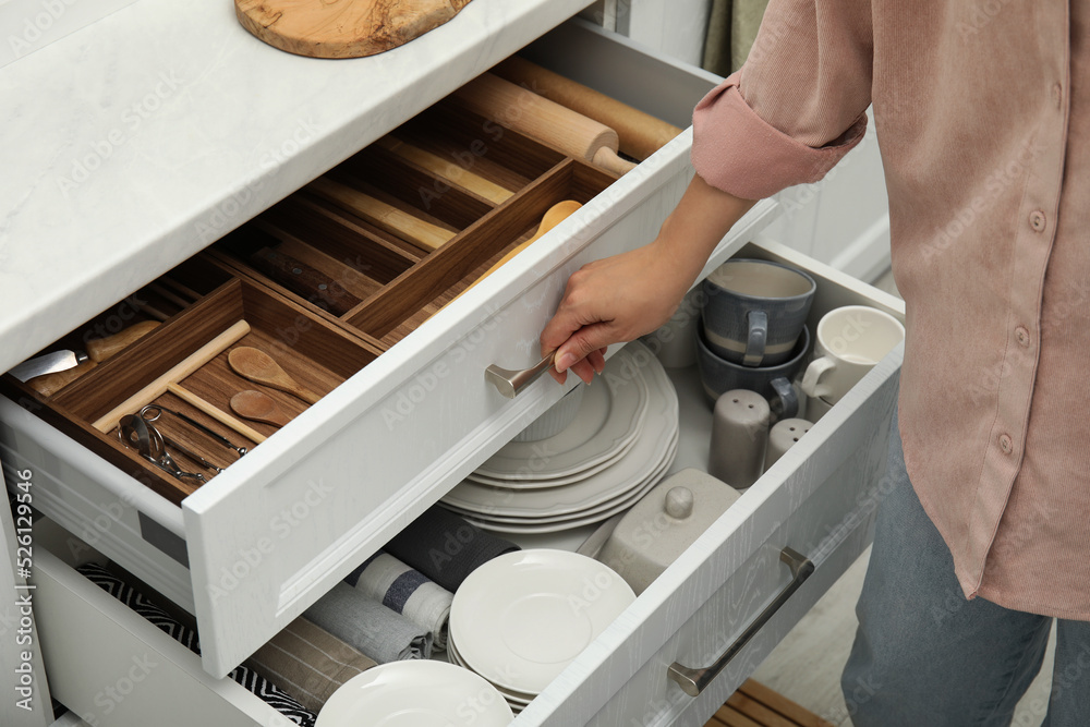 Woman opening drawers of kitchen cabinet with different dishware and ...