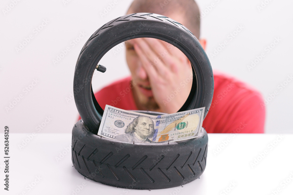100 dollars laying down on a two small scooter tire with sad man ...