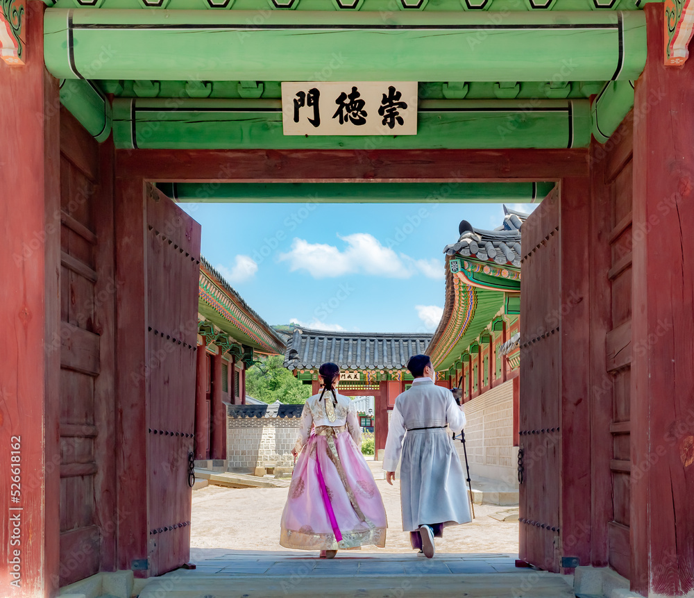 Couple wearing traditional Korean clothing hanbok by a colorful wooden ...
