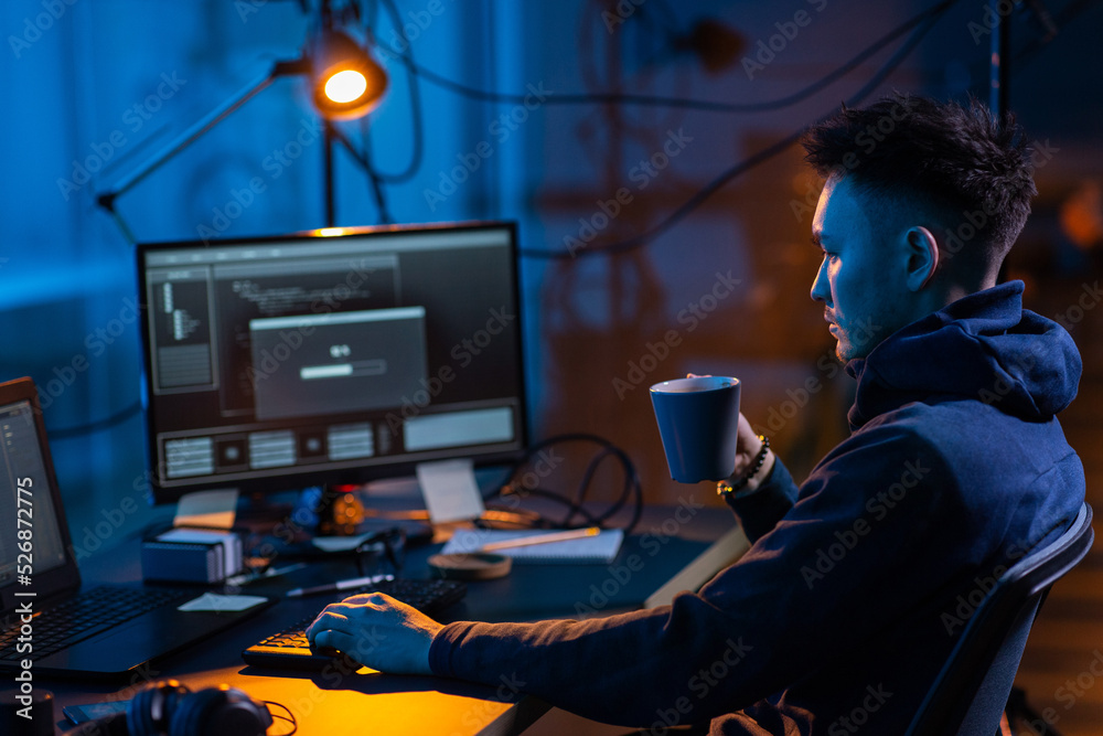 cybercrime, hacking and technology concept - male hacker in dark room drinking coffee and using ...