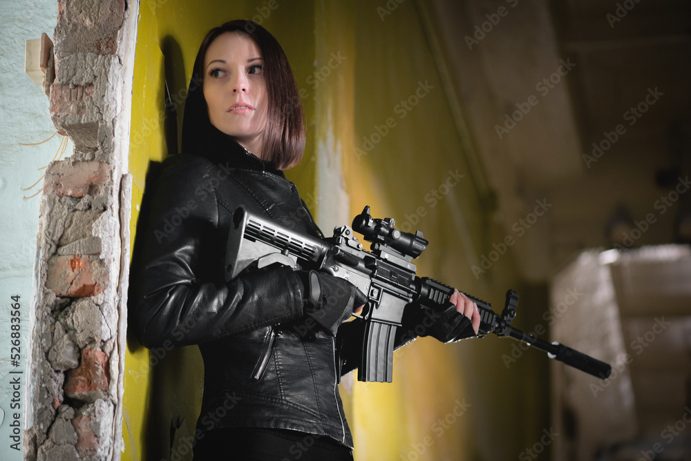 Young woman with the airsoft rifle is posing in the abandoned building ...