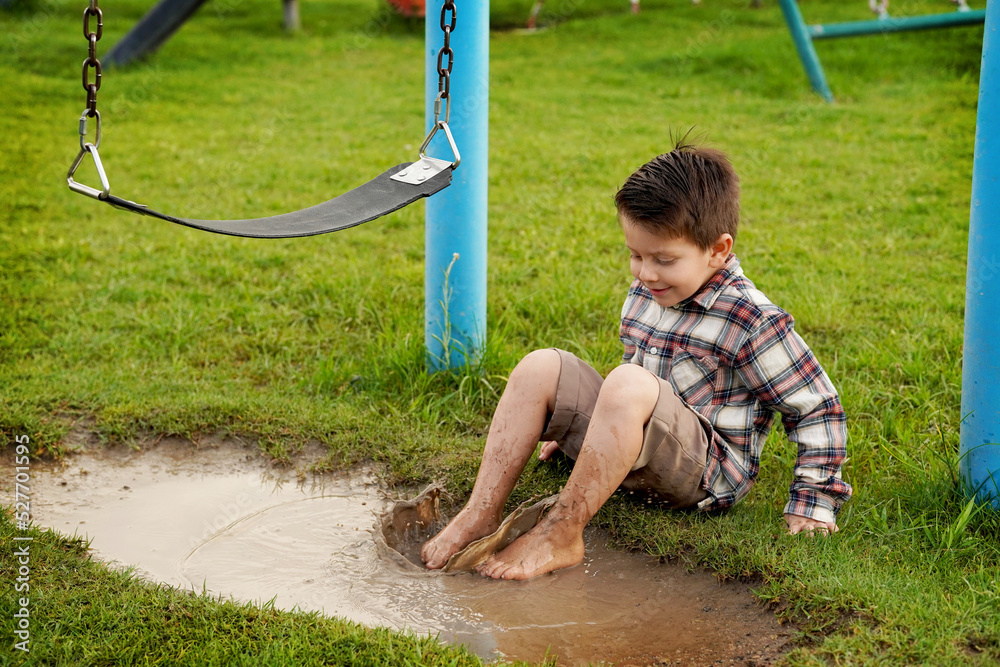 Niño feliz sentado mojando sus pies en un charco de agua con lodo y ...