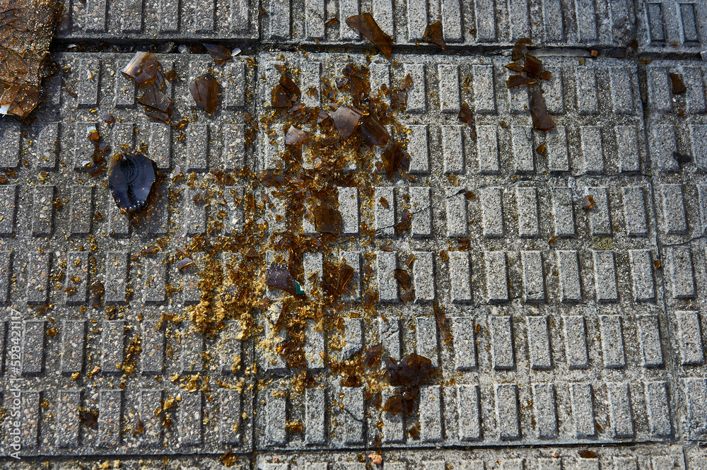 amber glass shards from a broken beer bottle on the concrete floor ...
