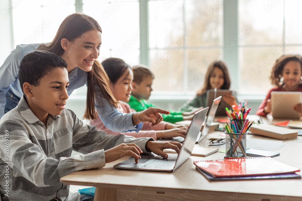 Teacher Teaching Diverse School Kids Using Laptop In Classroom Stock ...