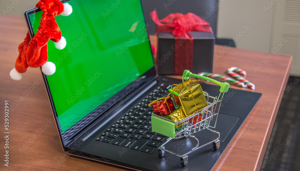 Shopping cart full of christmas gifts on laptop computer with green ...