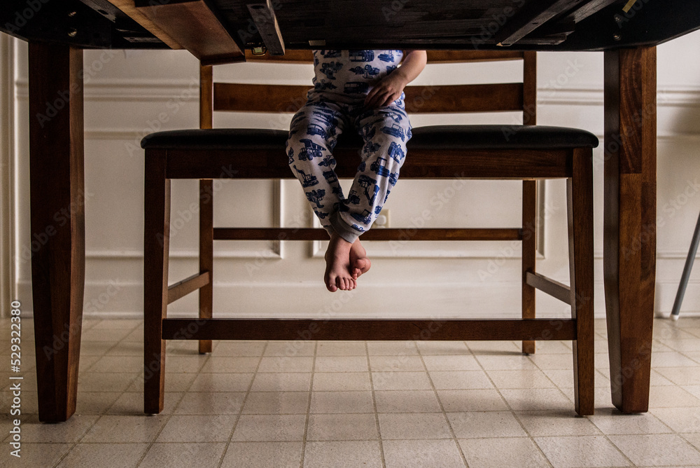 feet of young boy dangling off tall bench seen from underneath table ...