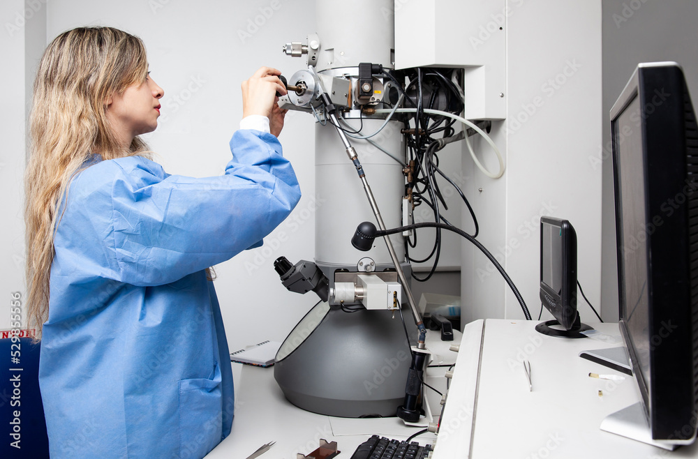Young female scientist loading a specimen using a sample holder into a ...