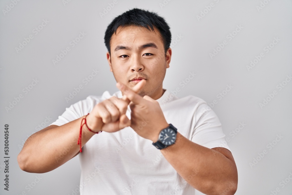 Young chinese man standing over white background rejection expression ...