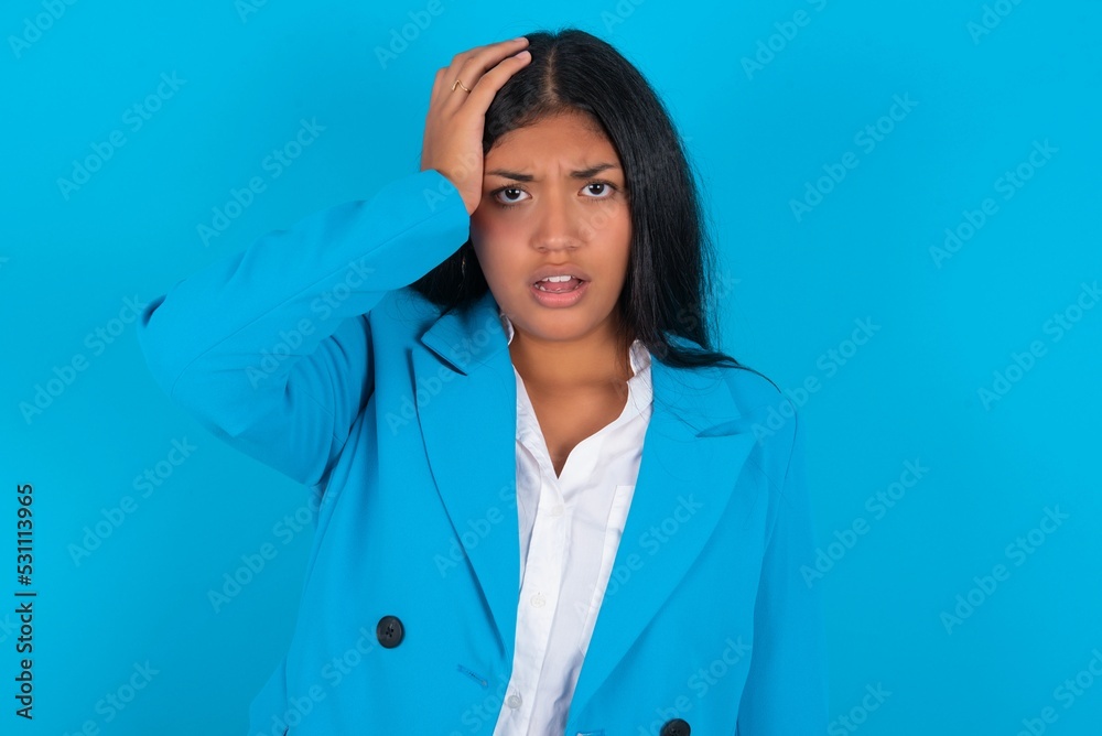 Embarrassed Young latin woman wearing blue blazer blue background with ...