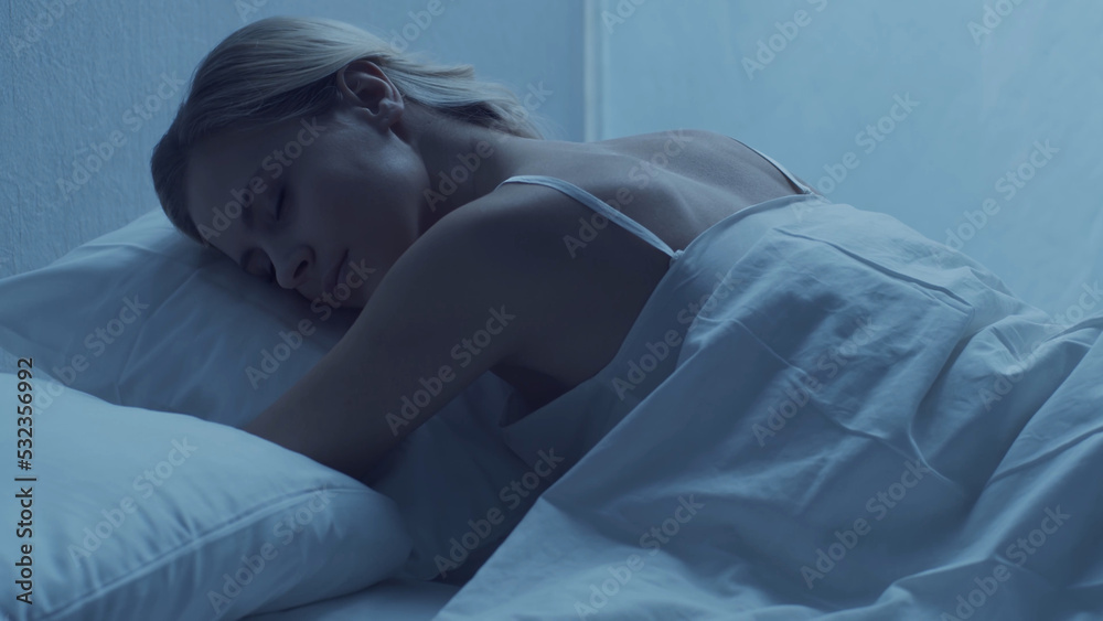 Young woman lying in the bed at night. Beautiful blond sleeping girl ...