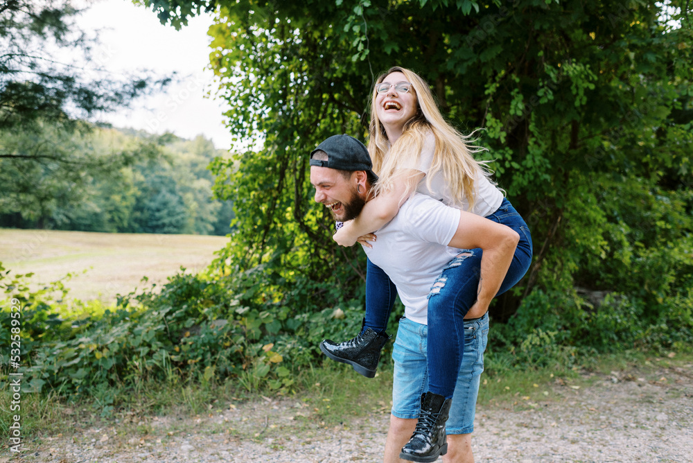 happy man laughing with his fiancé as he gives her a piggy back ride ...