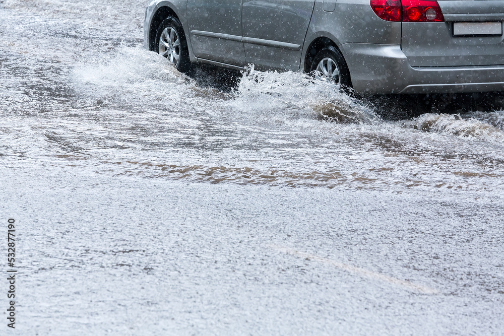 car driving through rain puddles with splashing water on flooded street ...