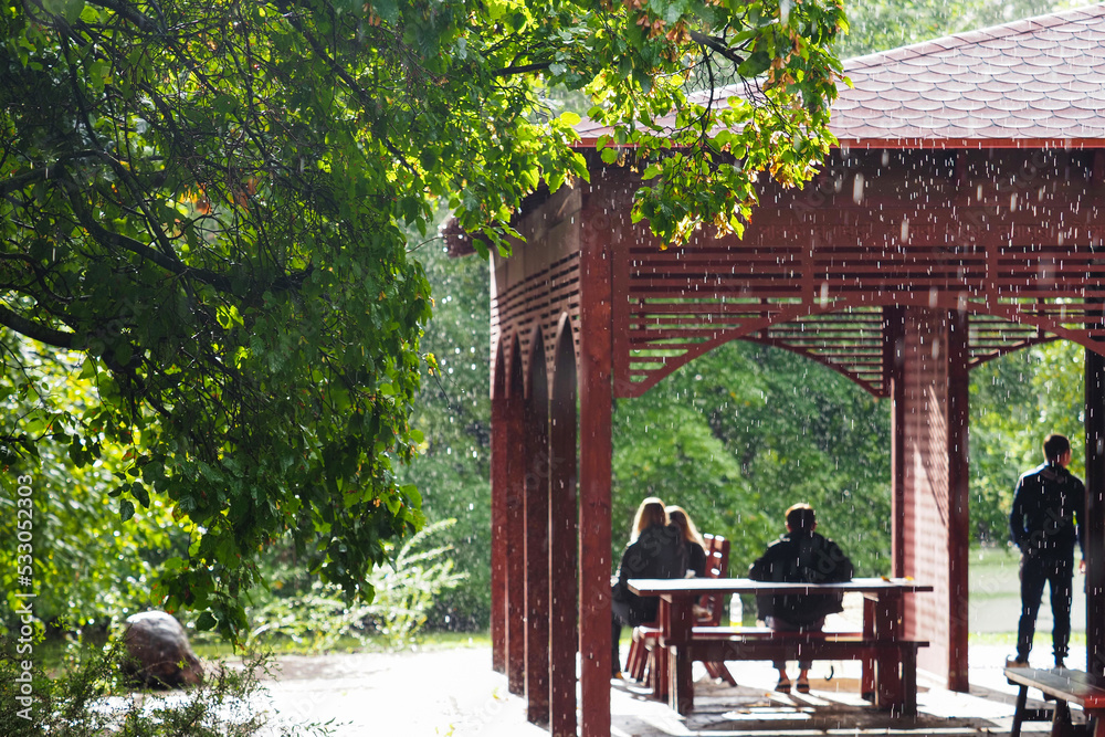 People hiding from the rain under roof of asian style wooden pergola ...