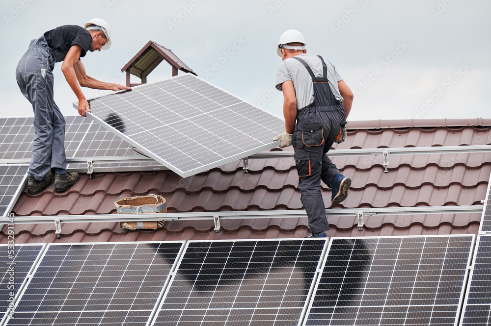 Men technicians lifting up photovoltaic solar moduls on roof of house ...