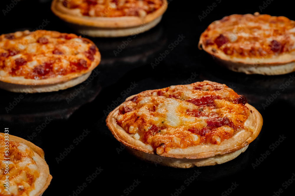 Many baked mini pizzas with ham, cheese on tray in electric oven ...