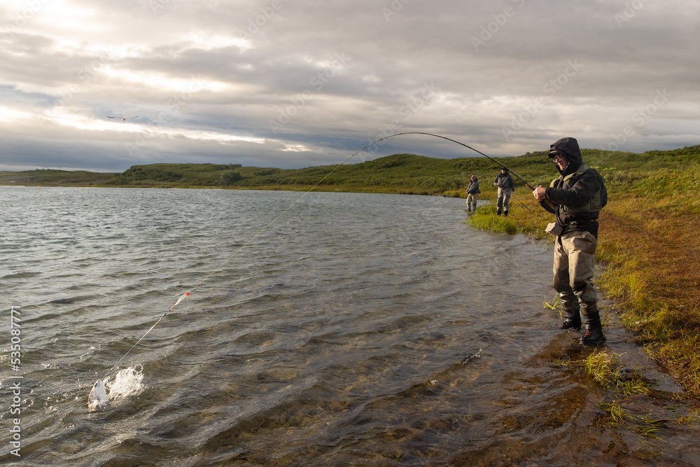 Man wearing waders fighting a Coho salmon on his fishing pole in the ...