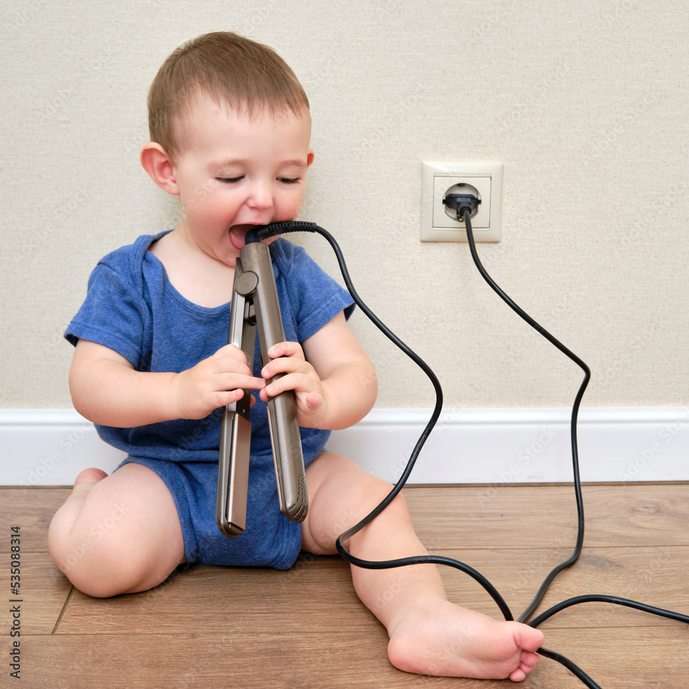 Child boy chewing on the electric wire of a curling iron. Toddler baby ...