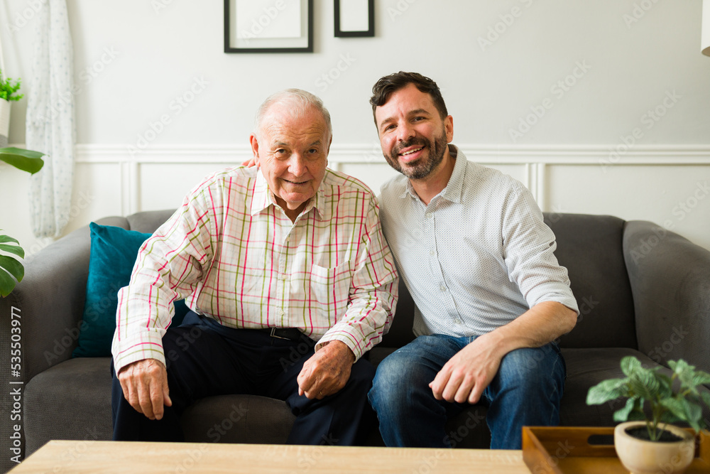 Cheerful old father and smiling young son hugging and relaxing at home ...