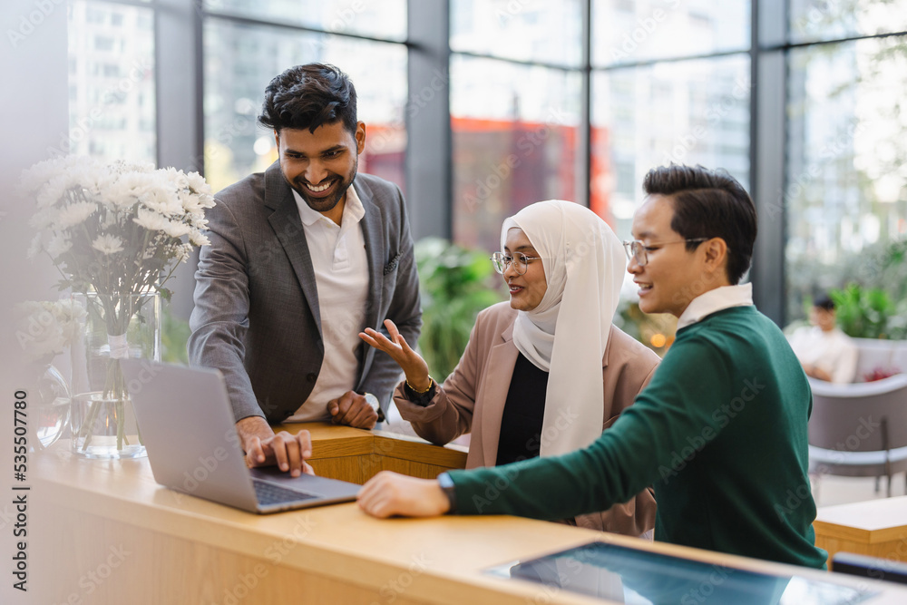 A diverse group of business people gather around a laptop in a modern ...