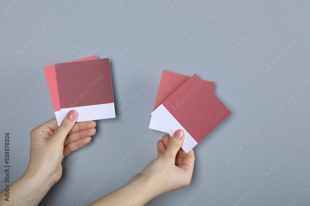 Woman with color sample cards choosing paint shade near grey wall ...