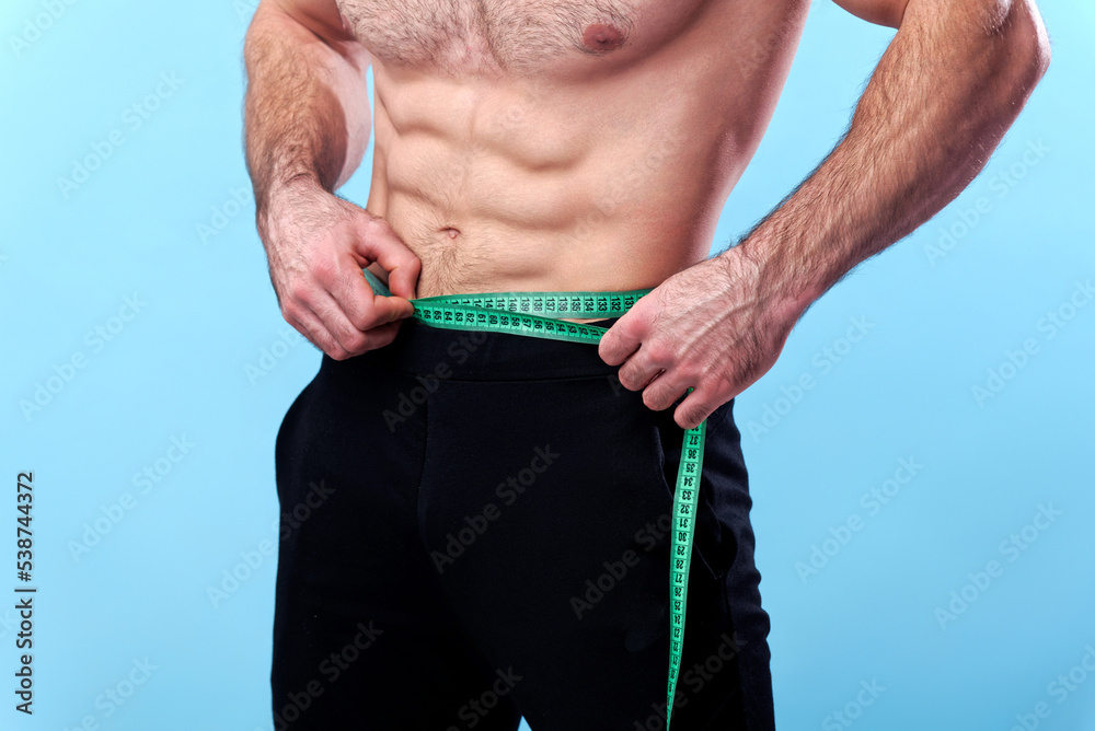 Strong bodybuilder measuring the width of his waist, putting a ...