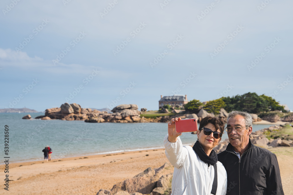 Older married couple taking a selfie on Renote Island in Tregastel. Brittany. France. Older ...