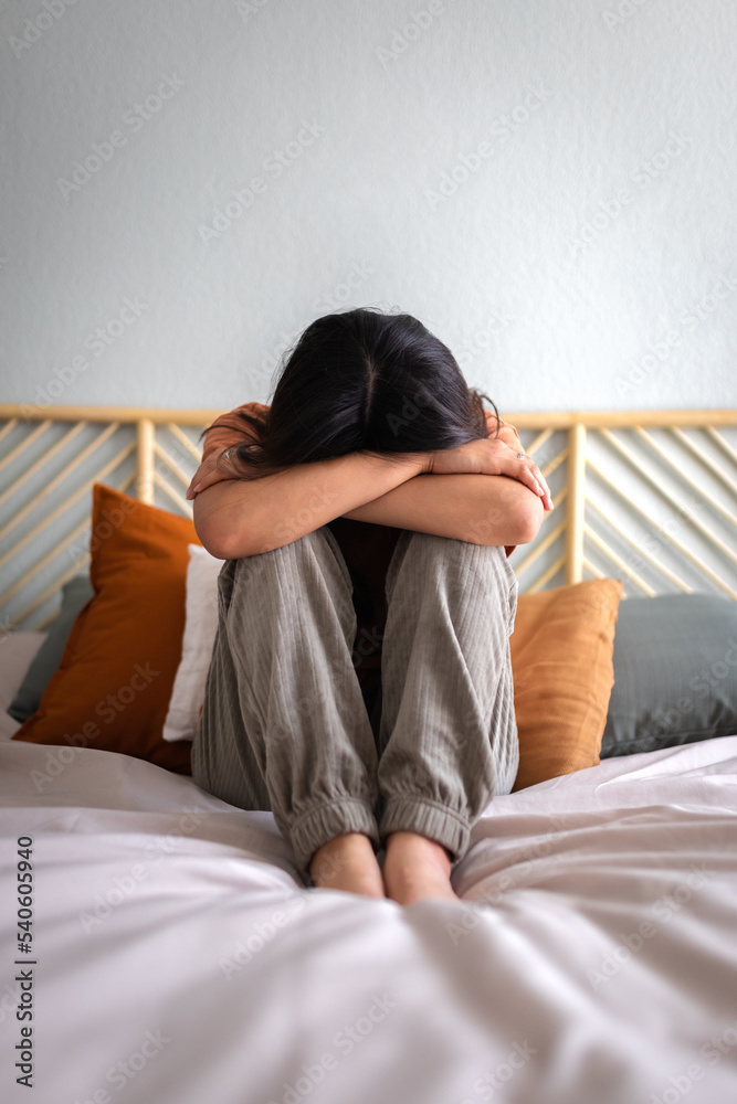 Front view of depressed and sad young woman sitting on the bed crying ...