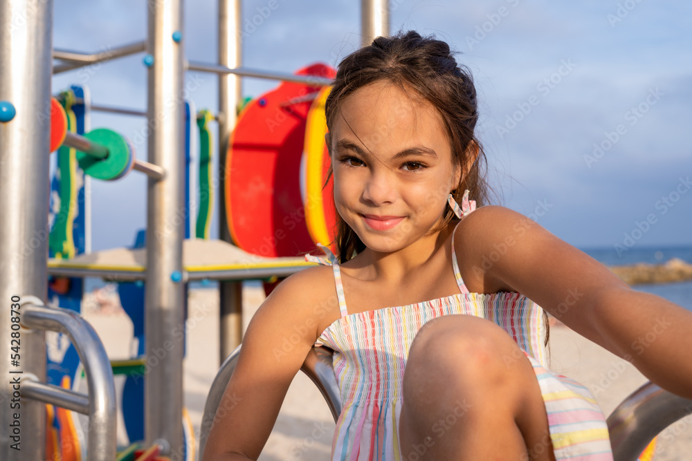 Little cute child girl in playground on the beach with smile on summer ...